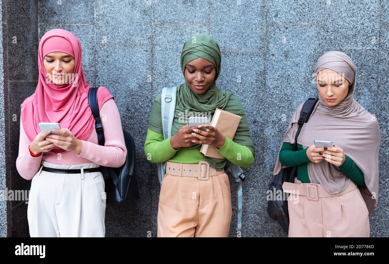 Three Modern Muslim Women Using Cellphones Standing Over Gray Wall ...