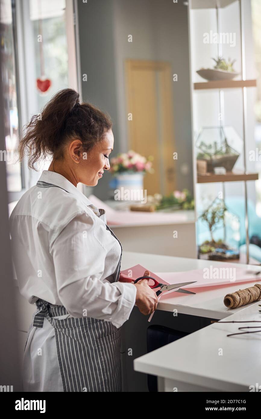 Professional flower shop worker cutting paper for wrapping a bouquet ...