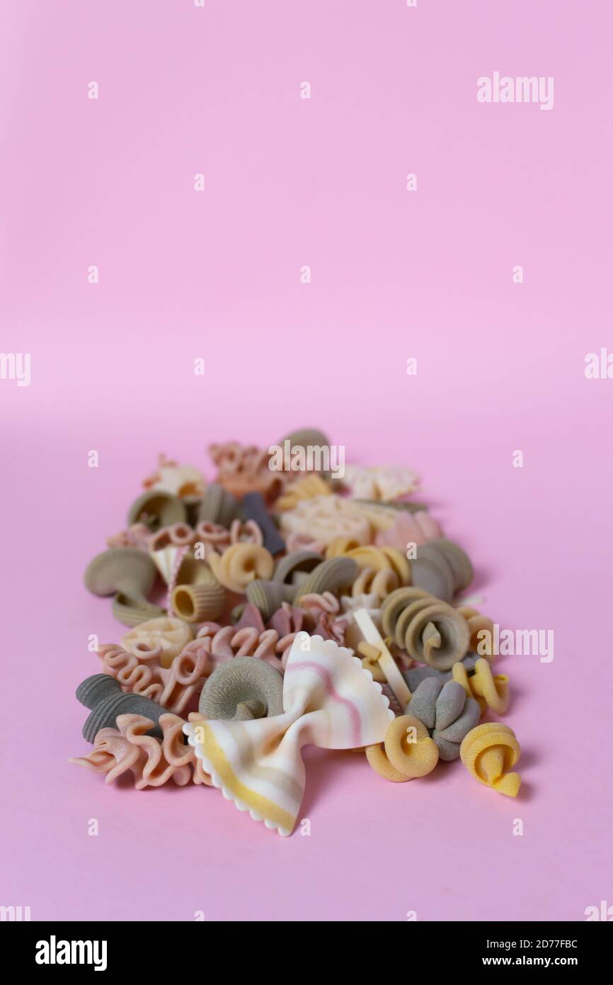 Italian pasta of different shapes and colors on a pink background. Copy ...