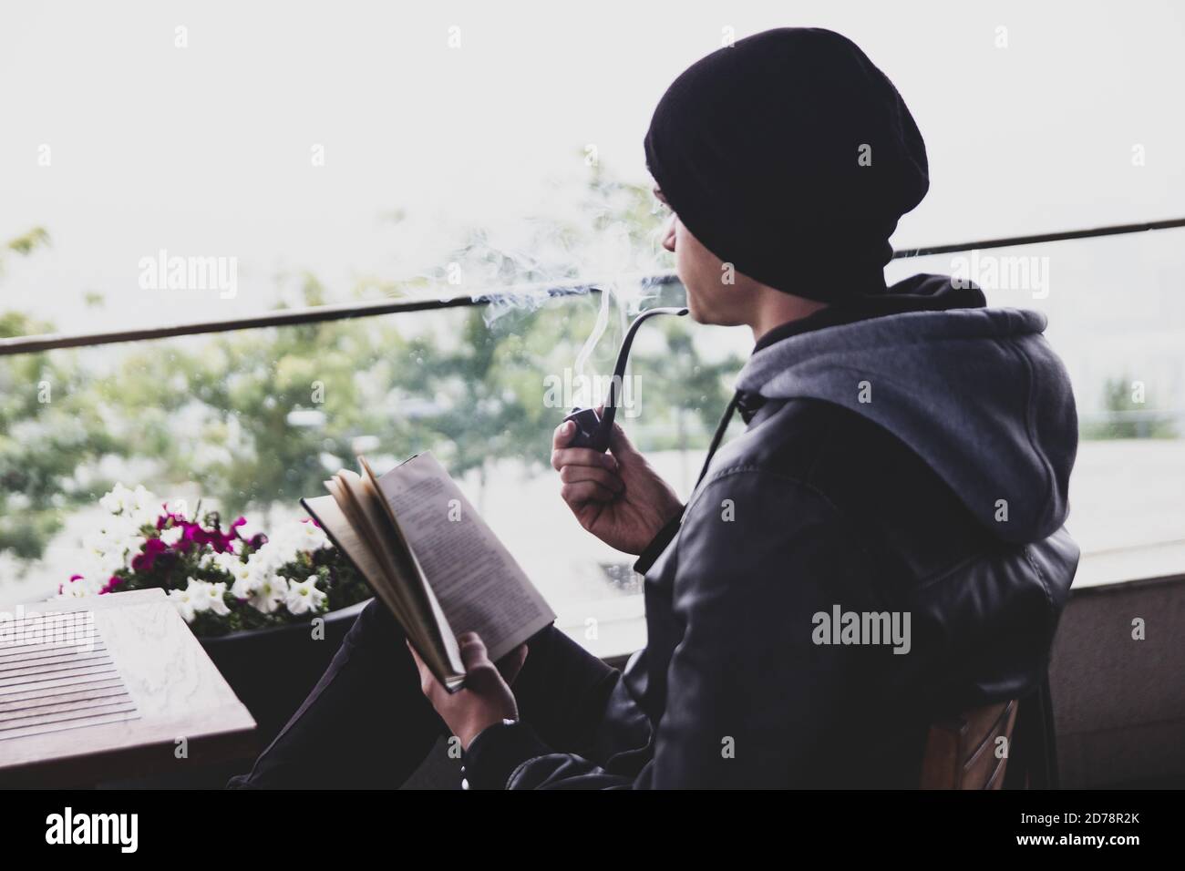 Back view on young black haired man witn piercing reeding a book and ...