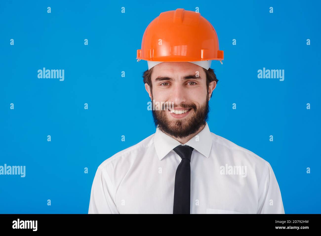 Young bearded civil engineer on blue isolated background. Studio ...