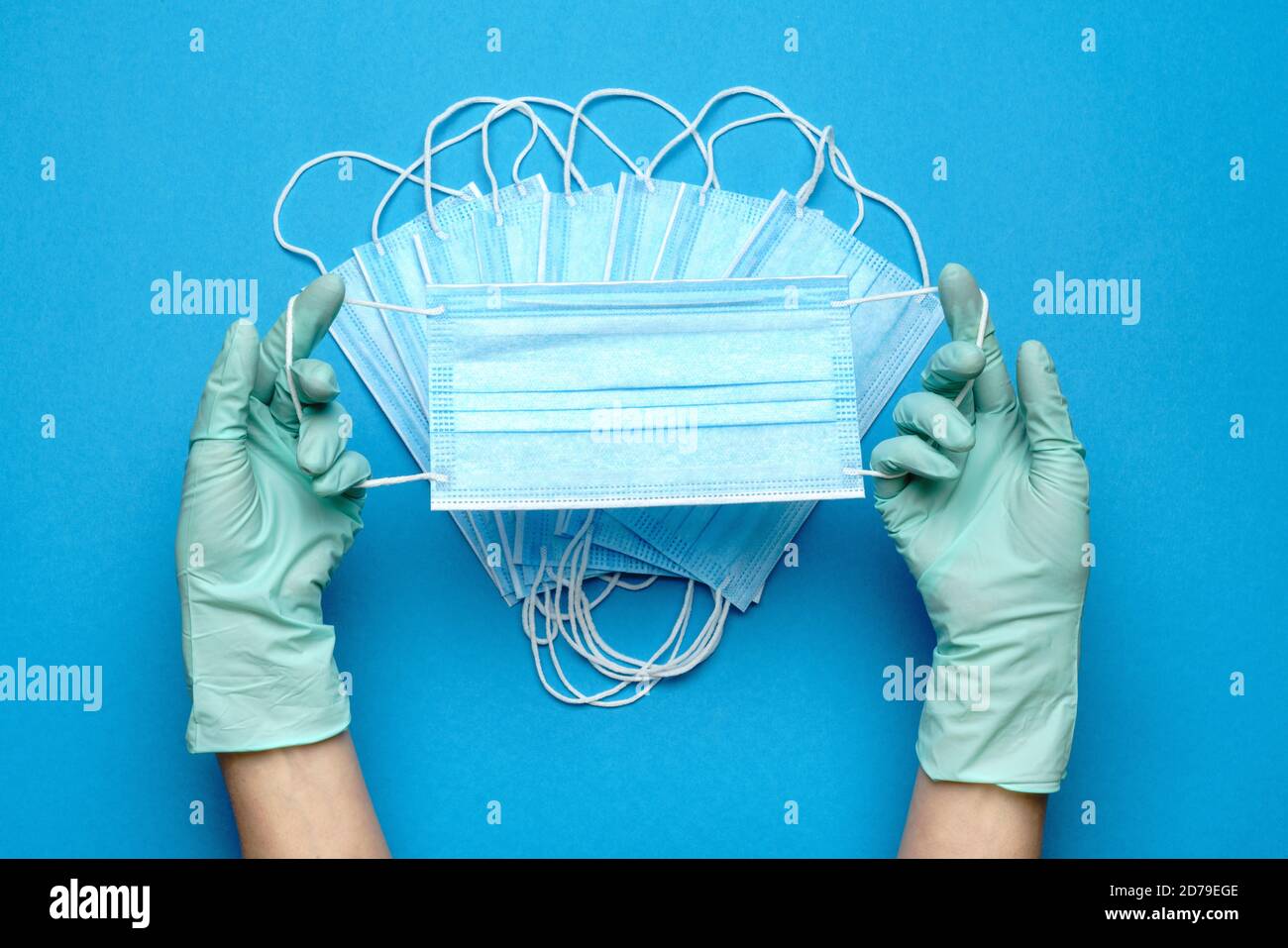 Human hand in protective gloves holding face protective mask over blue ...