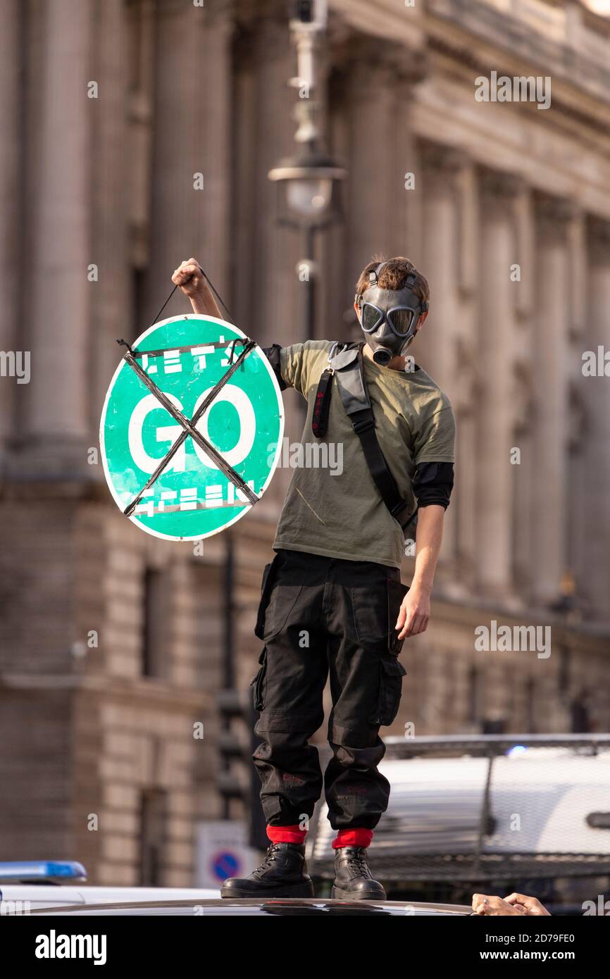 Protester in gas mask and holding sign stands on roof of car ...