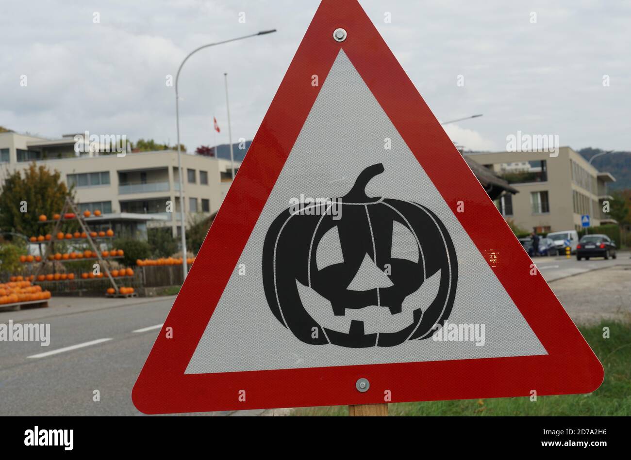 A triangle road sign with a carved pumpkin at the road side. In the ...
