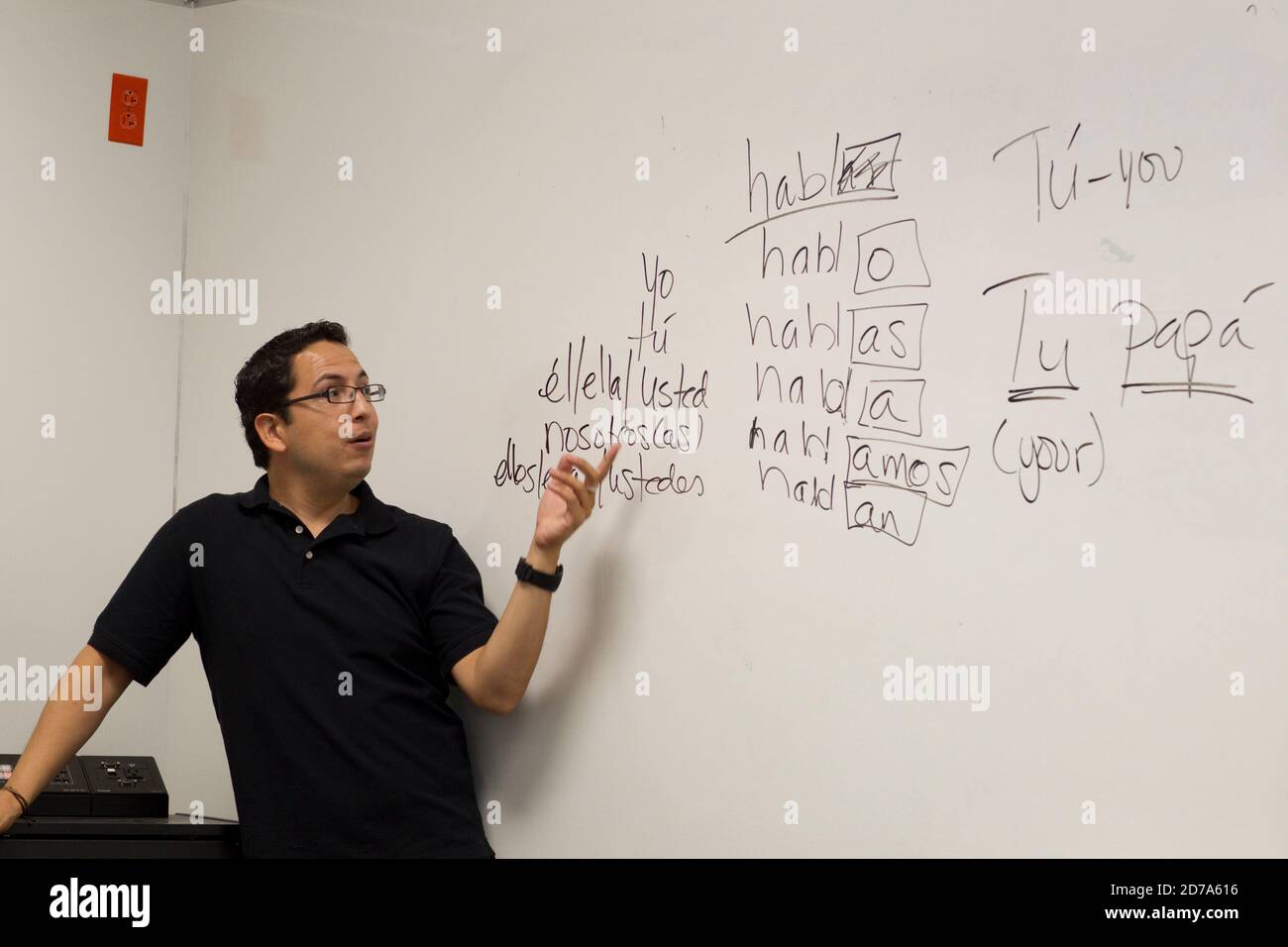 Hispanic teacher uses a whiteboard to conjugate a verb during Spanish ...