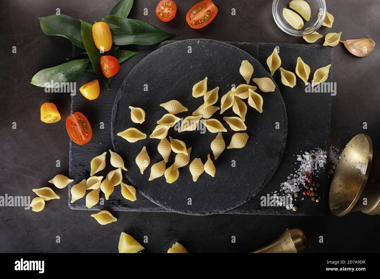 Pasta shells on black stone. Tomatoes and bay leaves with allspice and ...