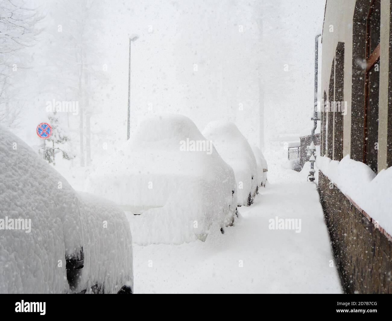 Cars heavily covered with snow stand in a row along the building during ...