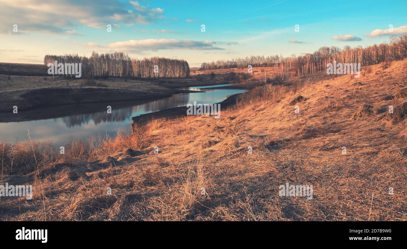 Sunny spring landscape with river and bare trees growing on the ...
