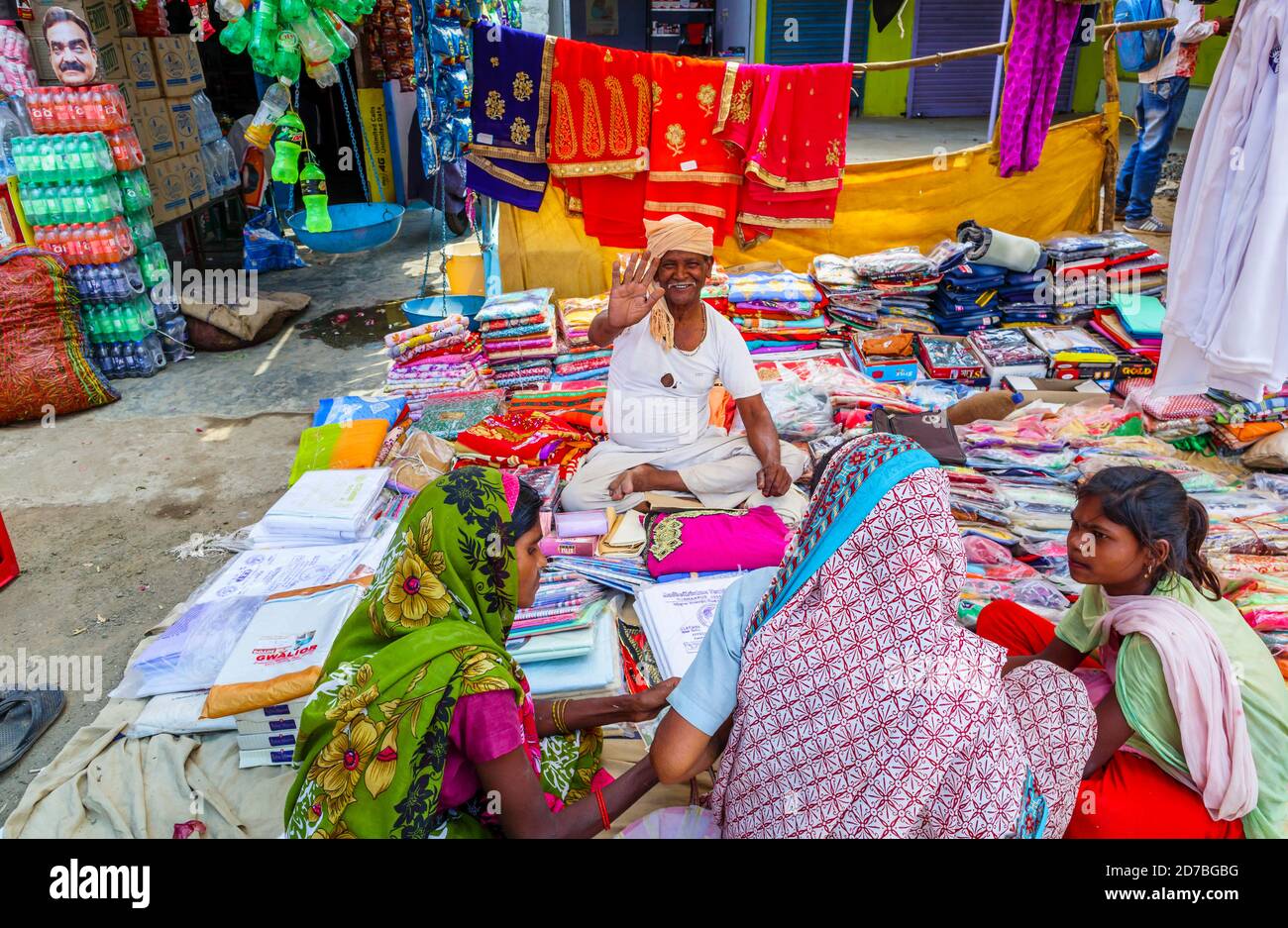 Friendly smiling stallholder sitting at a stall selling colourful ...