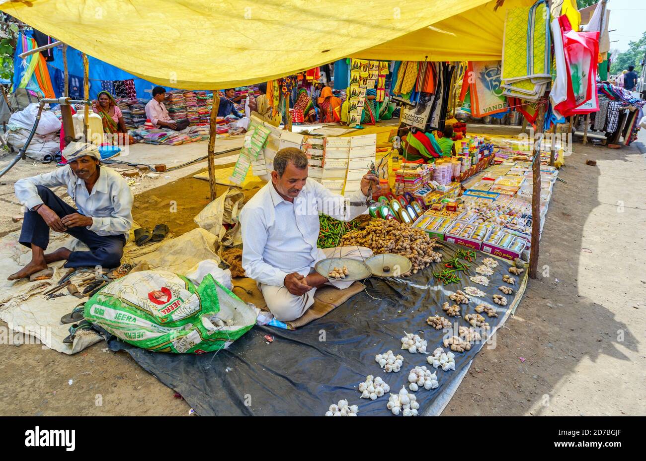 Stallholder sitting in a stall selling local produce weighing ginger on ...