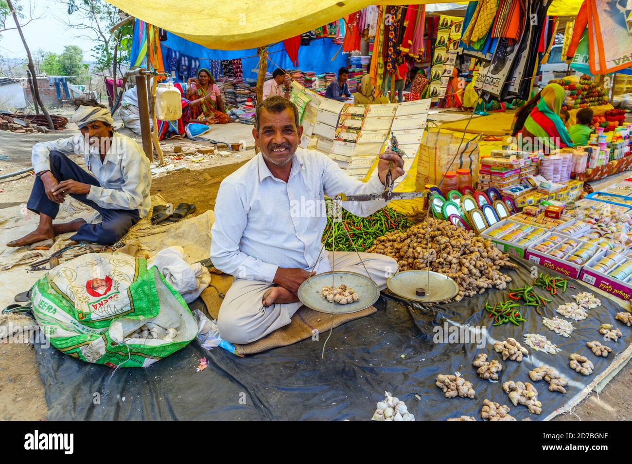 Stallholder sitting in a stall selling local produce weighing ginger on ...