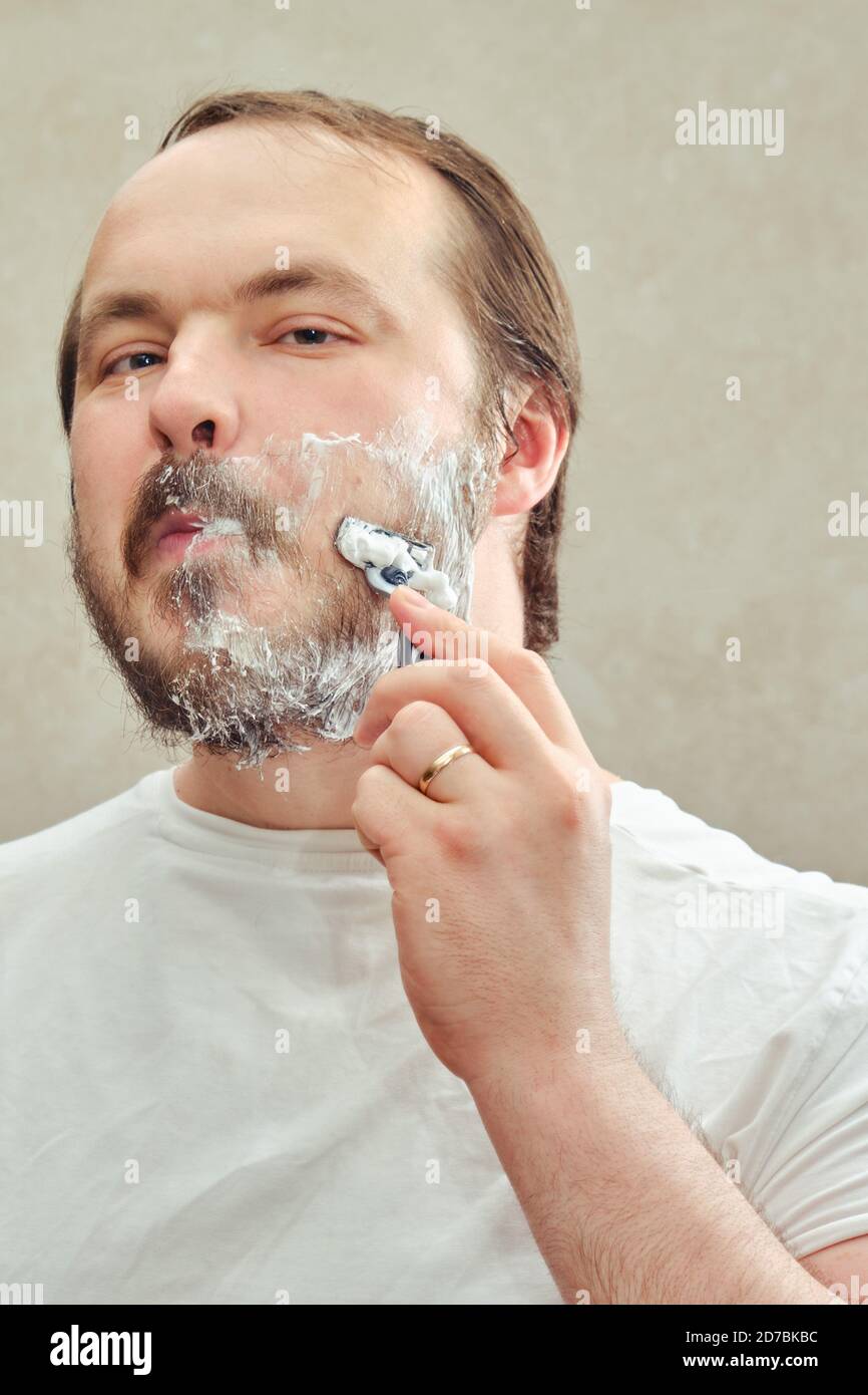 Portrait of a 35-40 year old man shaving his beard with a razor, close ...