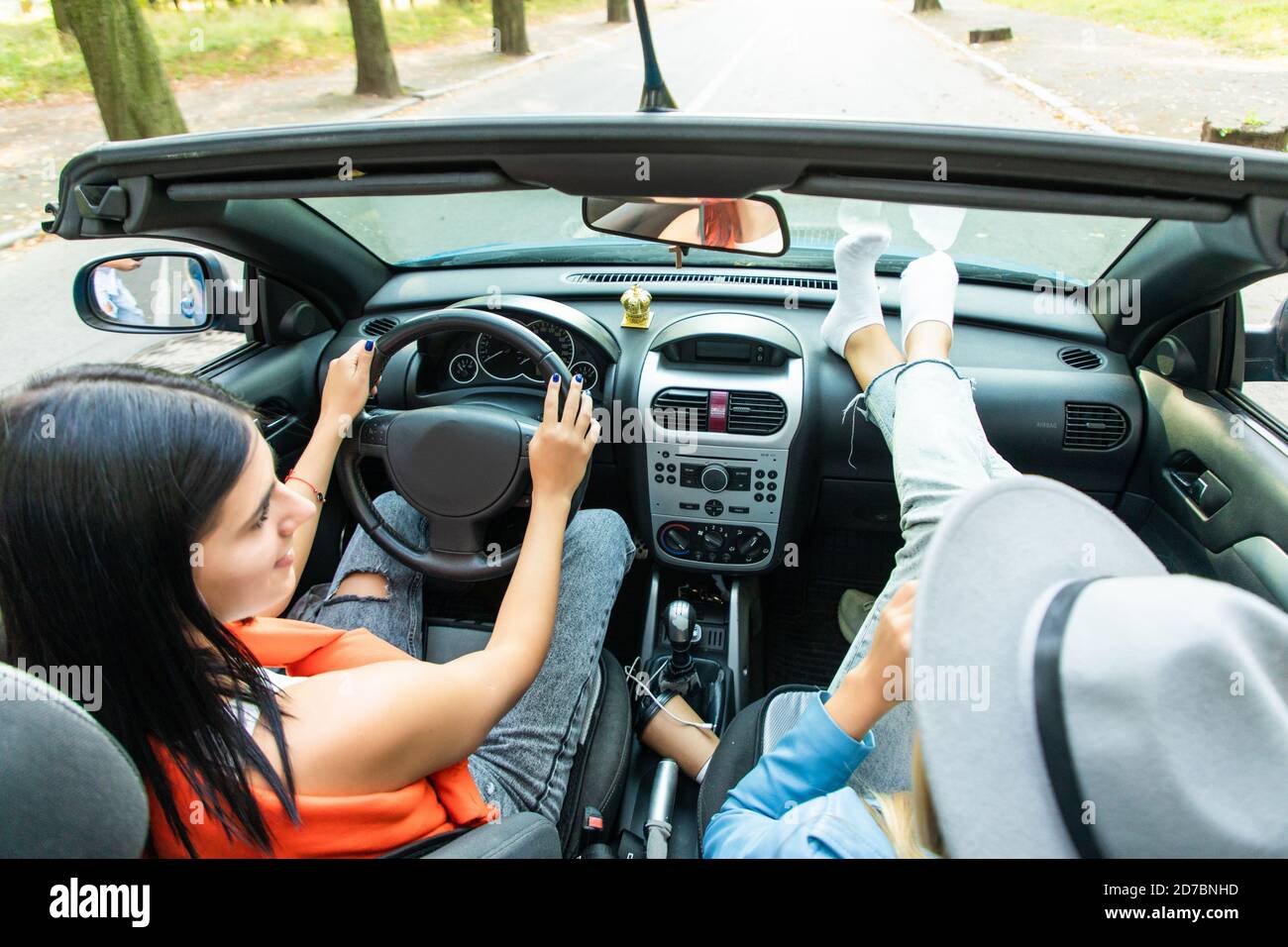 Rear view of two young women driving convertible car on summer road ...