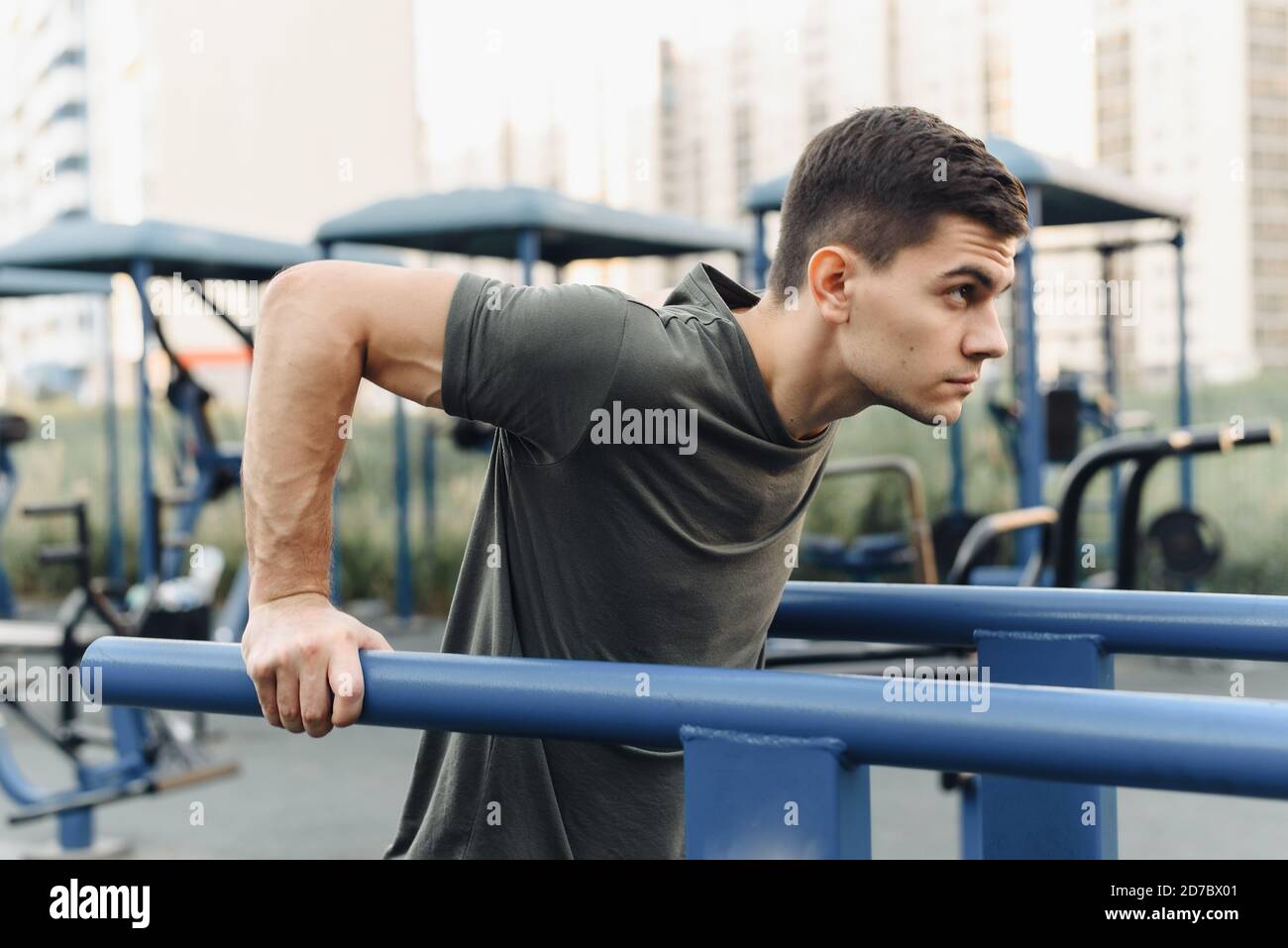 Handsome young man doing dips on the uneven bars on the outdoor sports ...