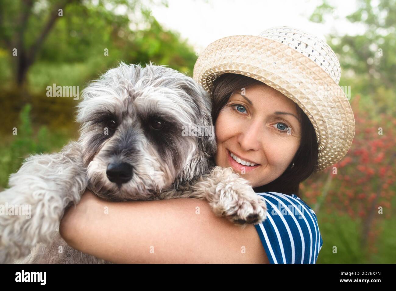 Image of beautiful middle-aged woman wearing straw hat looking aside while walking in green park ...