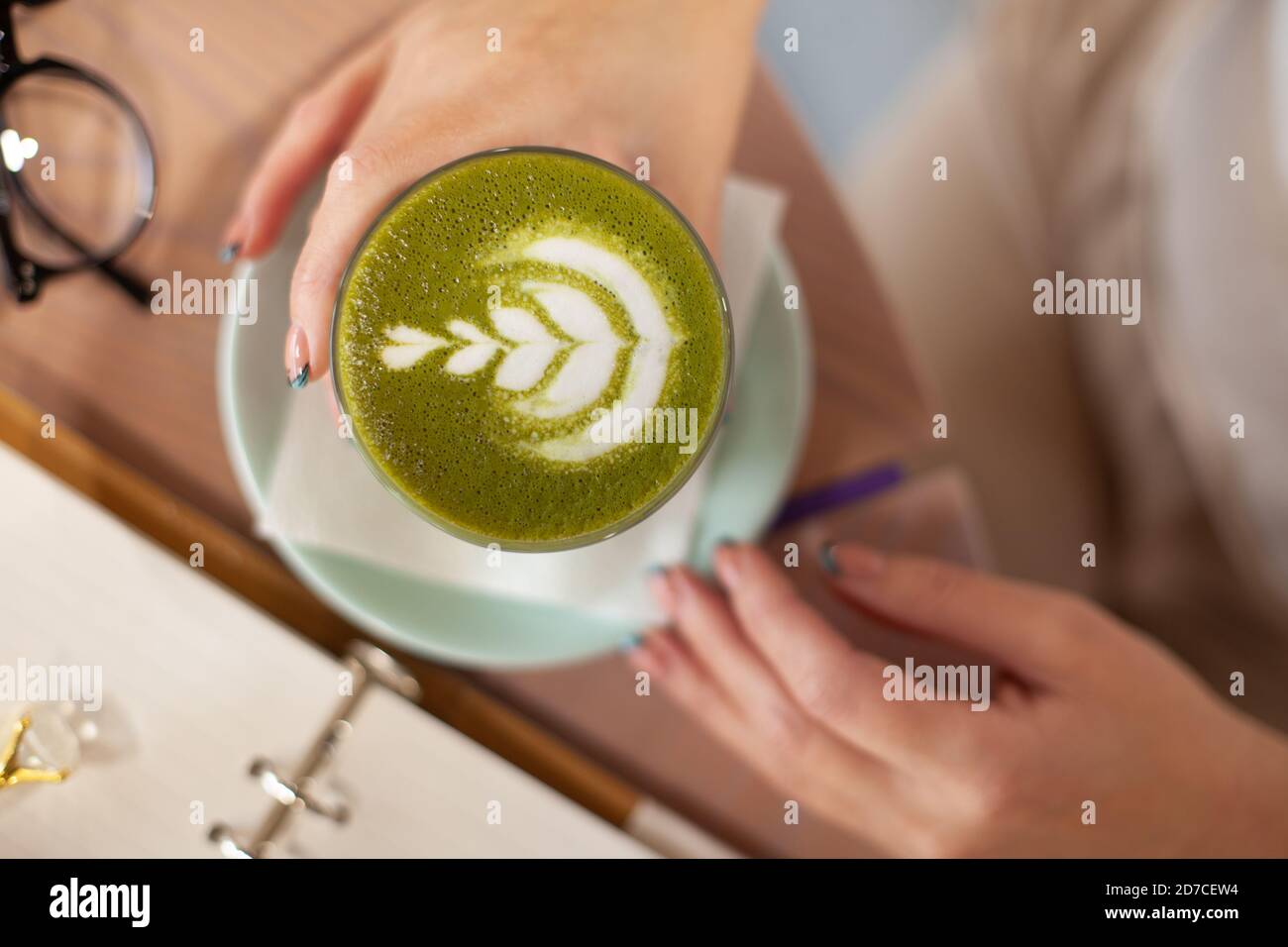 Top view glass of hot matcha green tea latte with art foam holding by woman hand on table Stock ...