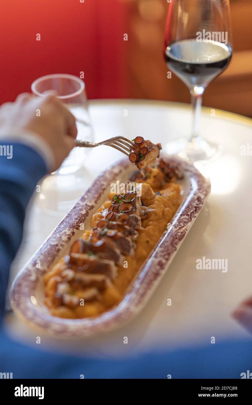 Vertical shot of a hand of a man eating tasty octopus and mash dish ...