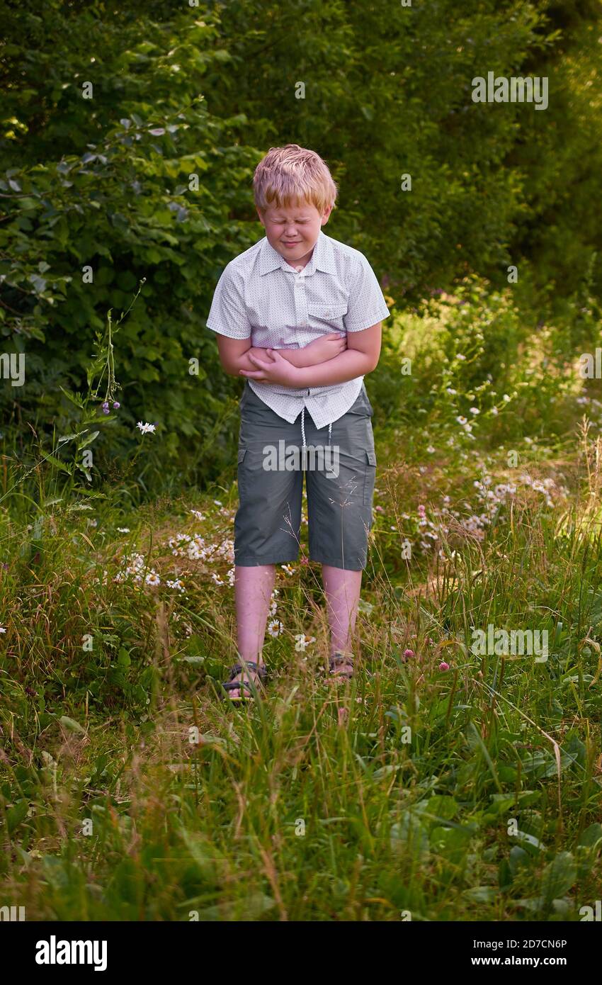 The boy holds his stomach and winces in pain in the Park Stock Photo ...
