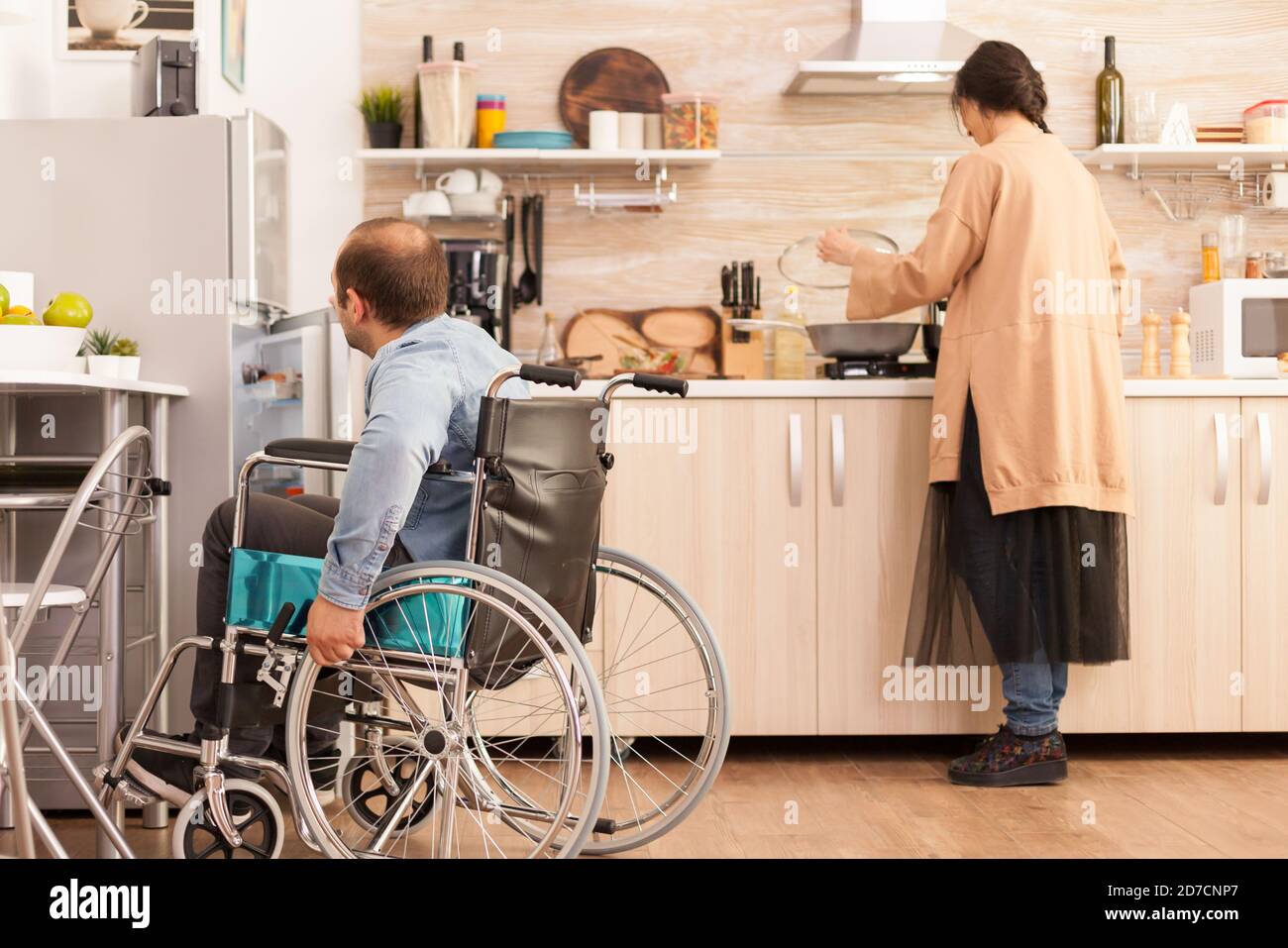 Disabled man in wheelchair opens refrigerator while wife is cooking ...