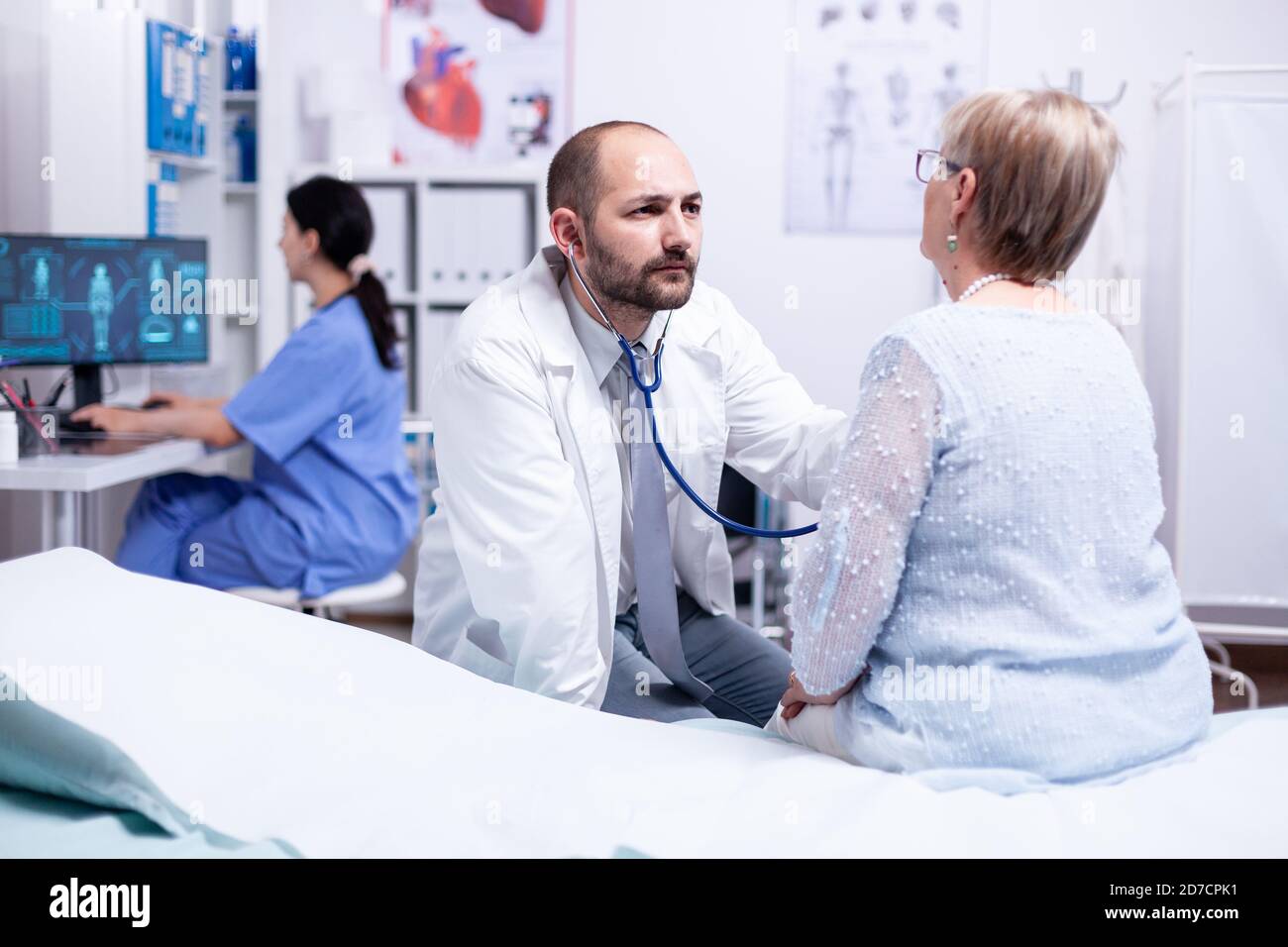 Elderly woman doctor appointment gets heart beat checked with stethoscope. Medical consultation ...