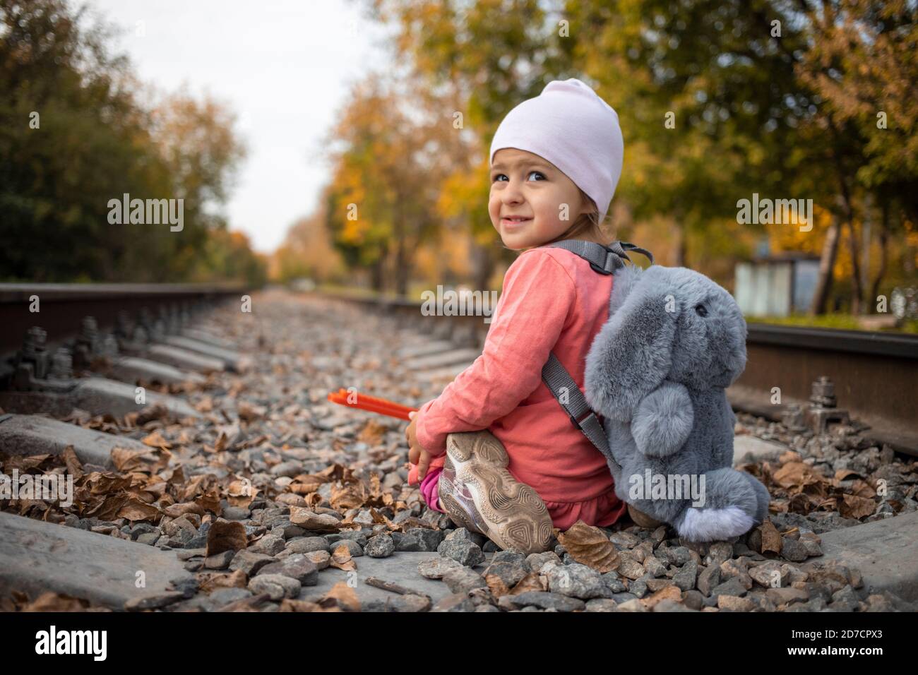 a cheerful hooligan girl sits on the railroad tracks and smiles slyly ...
