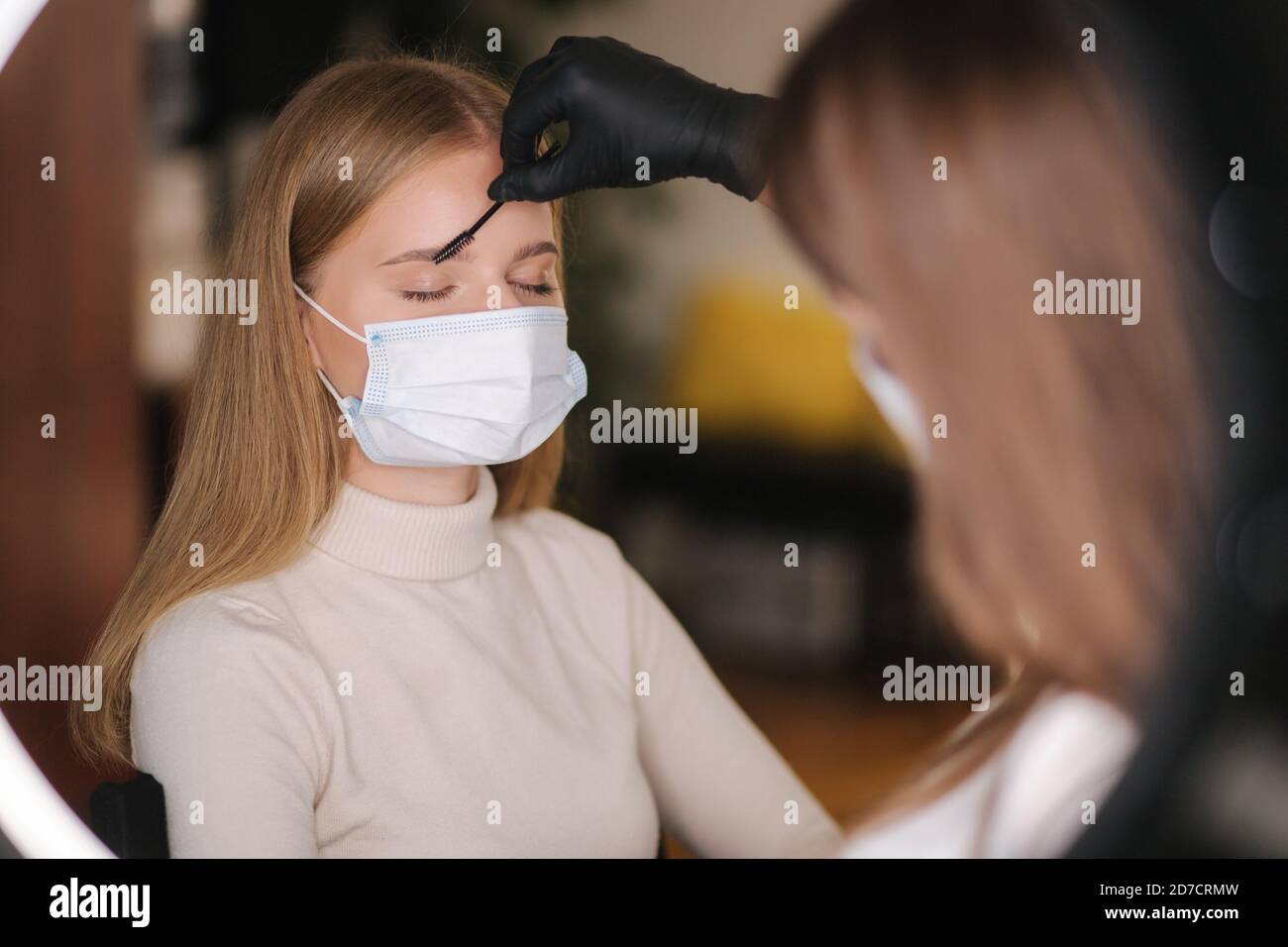 Brow and makeup master in protective mask gives shape to pull out with ...