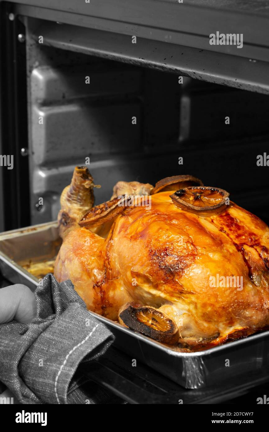 Man taking whole cooked chicken out of an oven with tea towel ...
