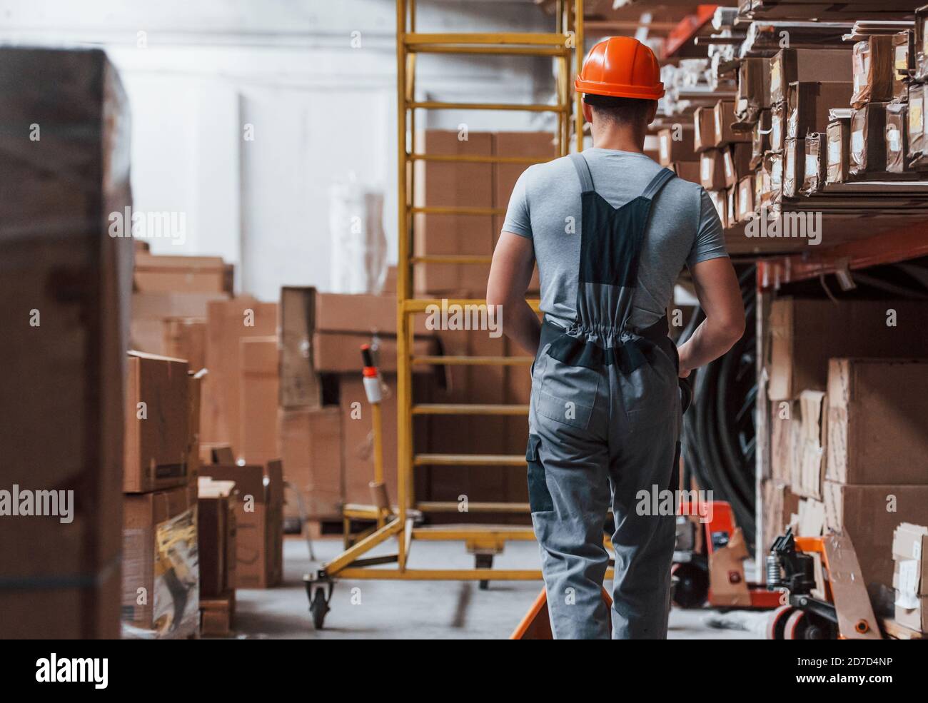 Young male worker in uniform is in the warehouse with pallet truck ...