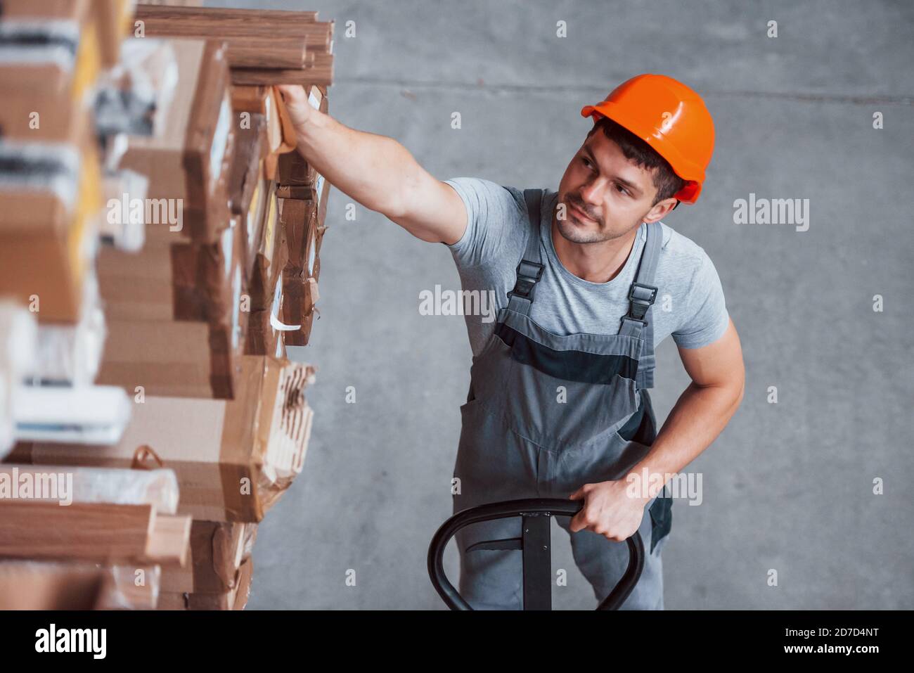 Young male worker in uniform is in the warehouse with pallet truck ...