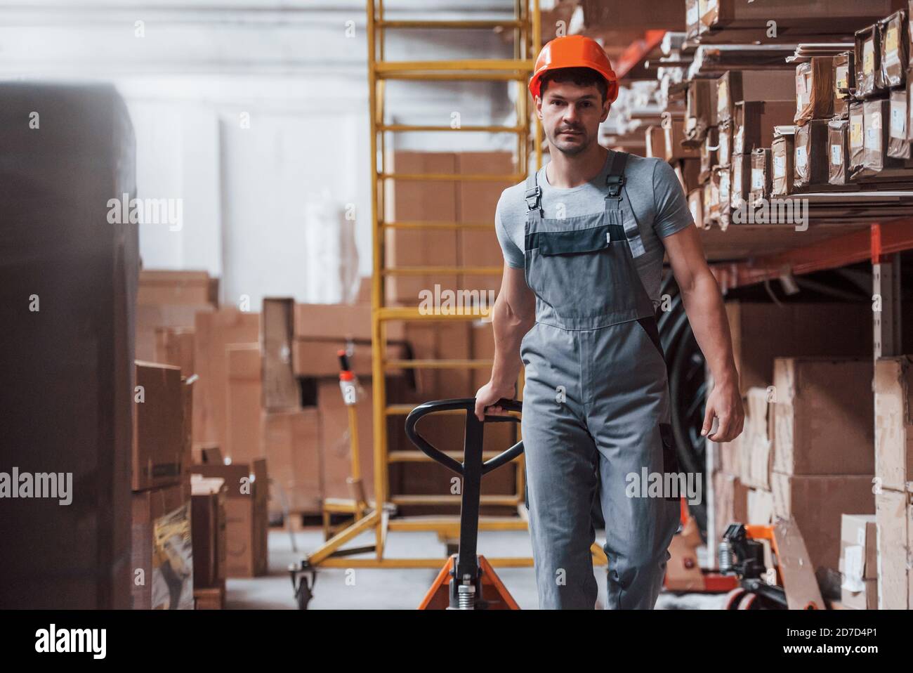 Young male worker in uniform is in the warehouse with pallet truck ...