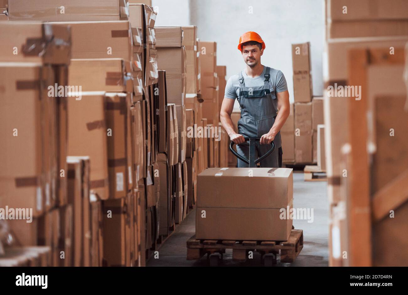 Young male worker in uniform is in the warehouse with pallet truck ...