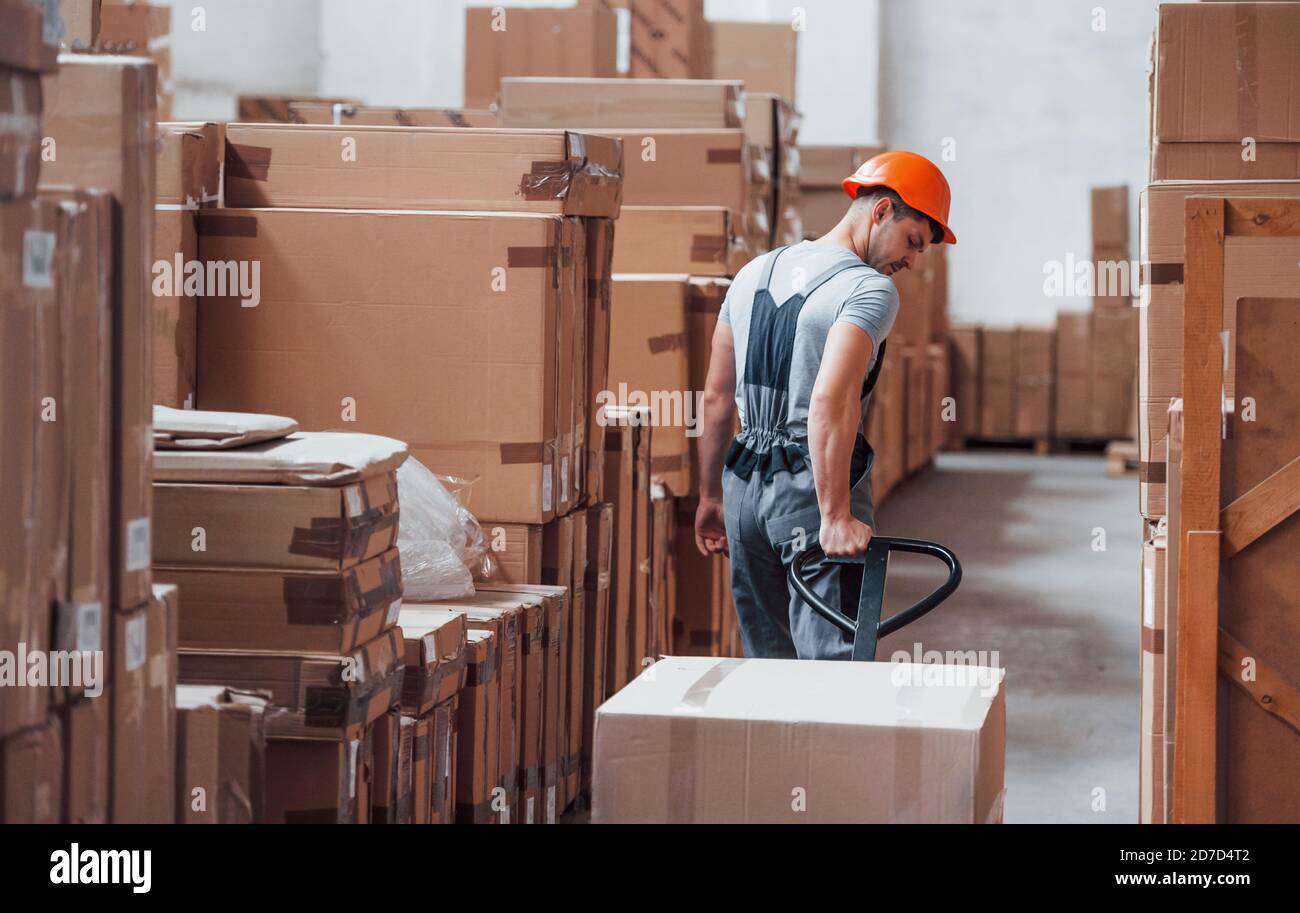 Young male worker in uniform is in the warehouse with pallet truck ...