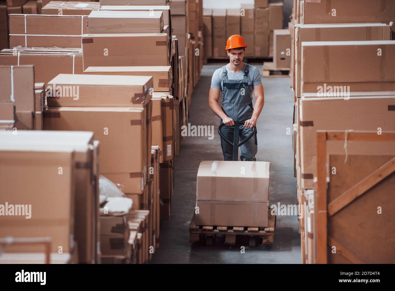 Young male worker in uniform is in the warehouse with pallet truck ...