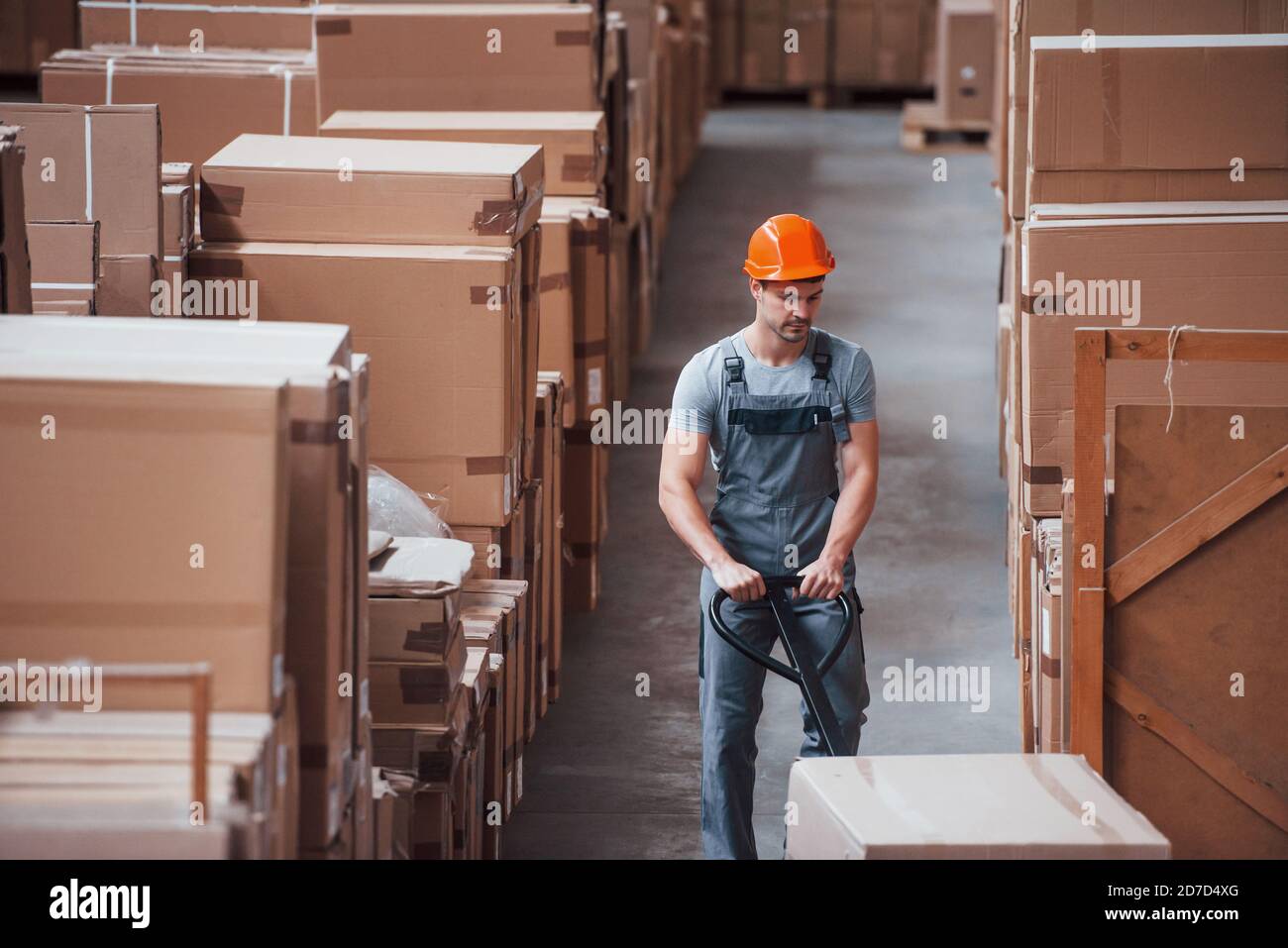 Young male worker in uniform is in the warehouse with pallet truck ...
