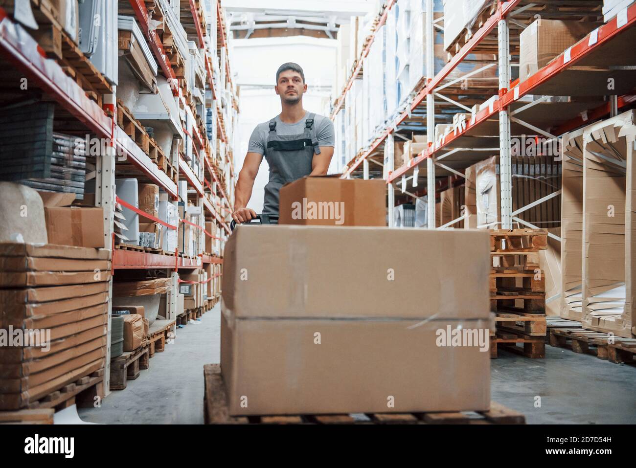 Young male worker in uniform is in the warehouse pushing pallet truck ...