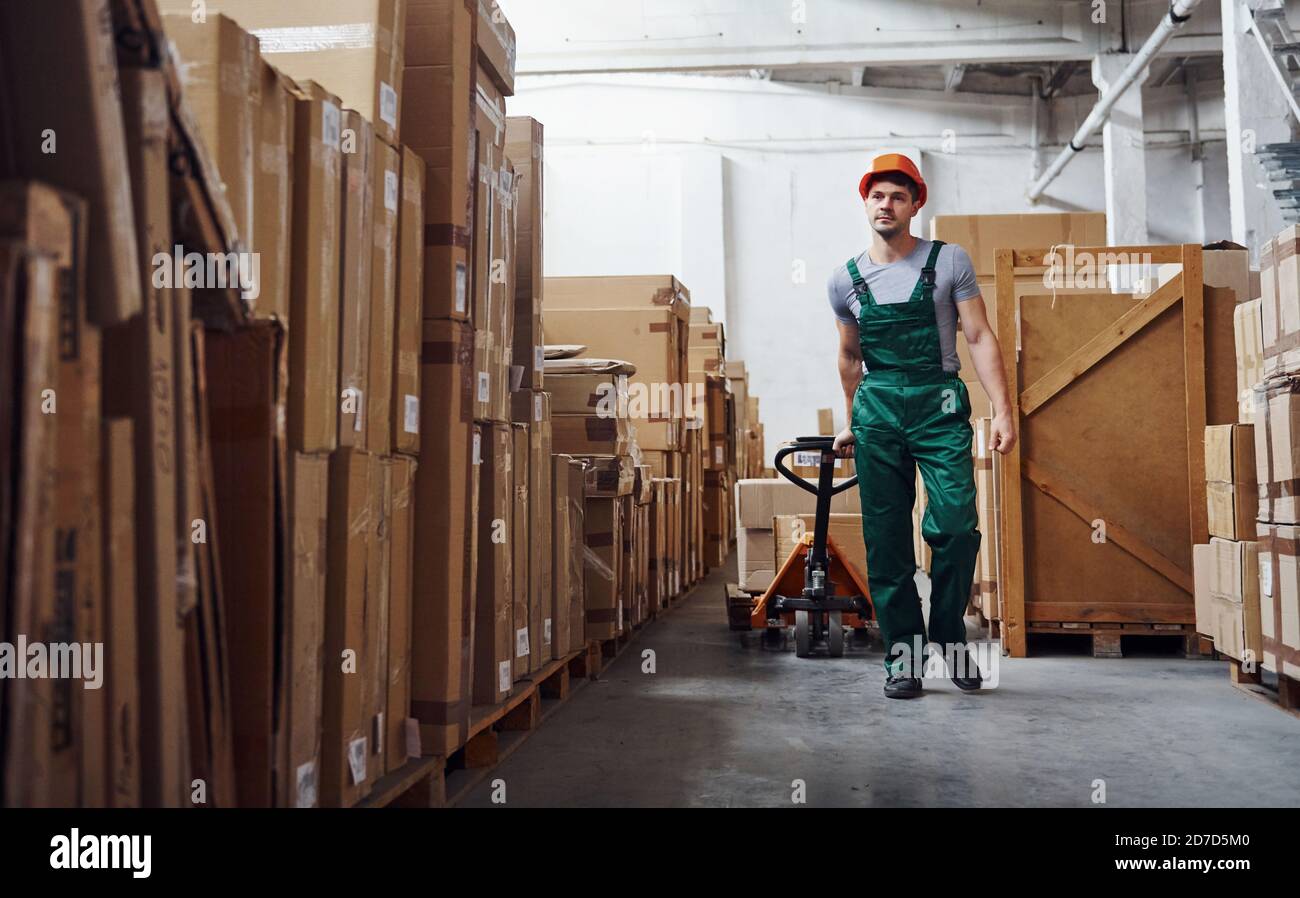 Young male worker in uniform is in the warehouse with pallet truck ...
