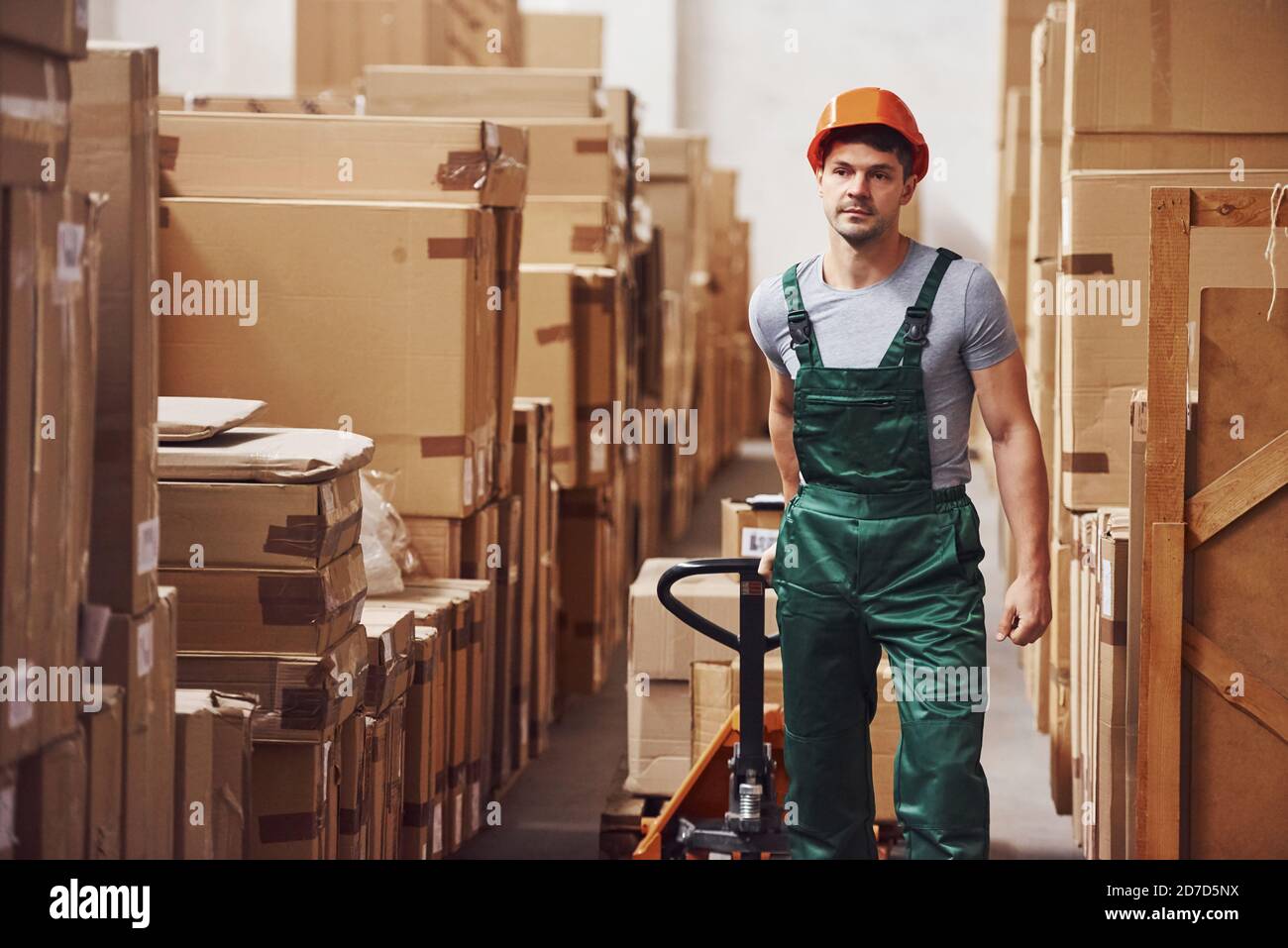 Young male worker in uniform is in the warehouse with pallet truck ...