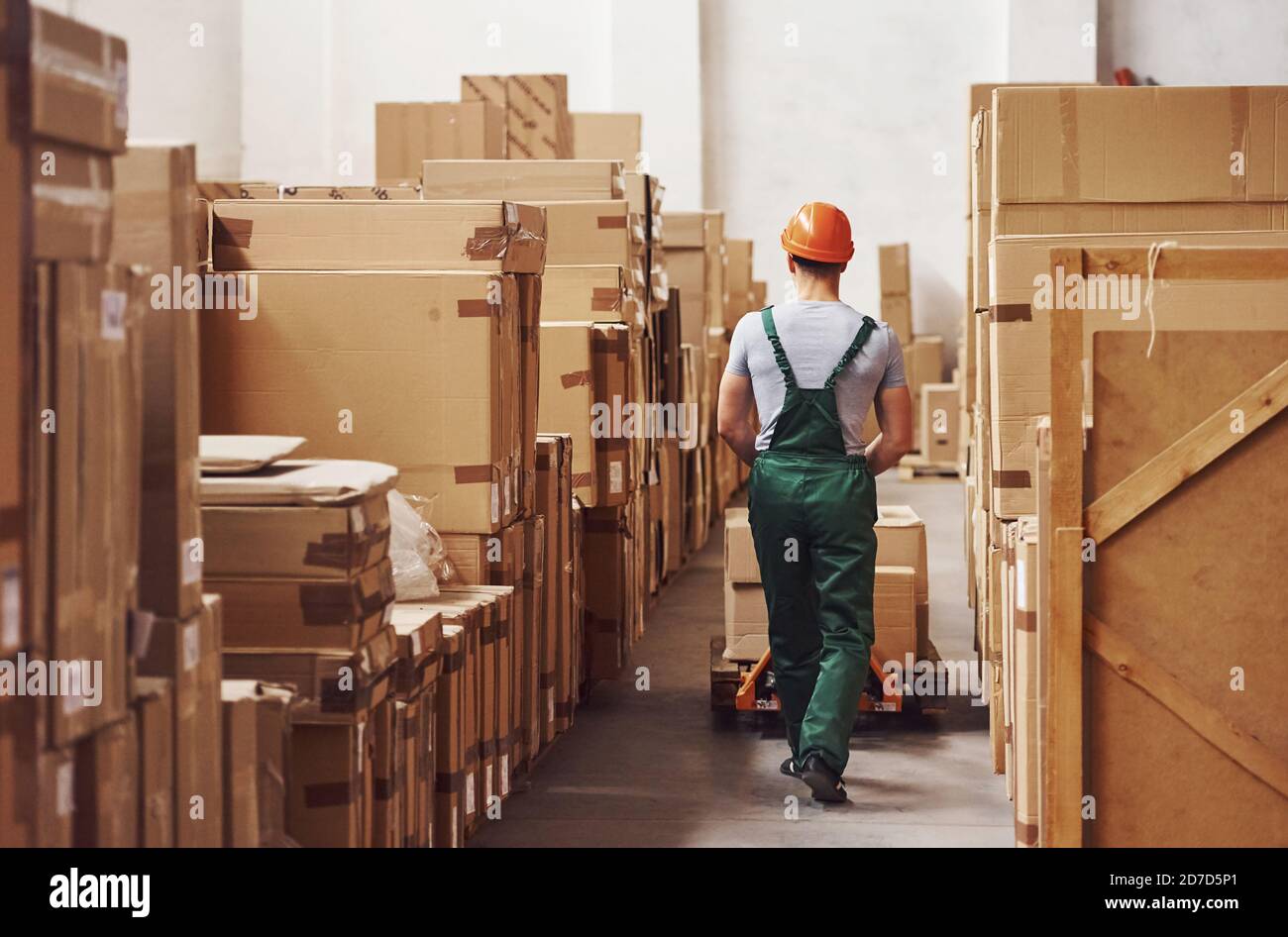 Young male worker in uniform is in the warehouse with pallet truck ...