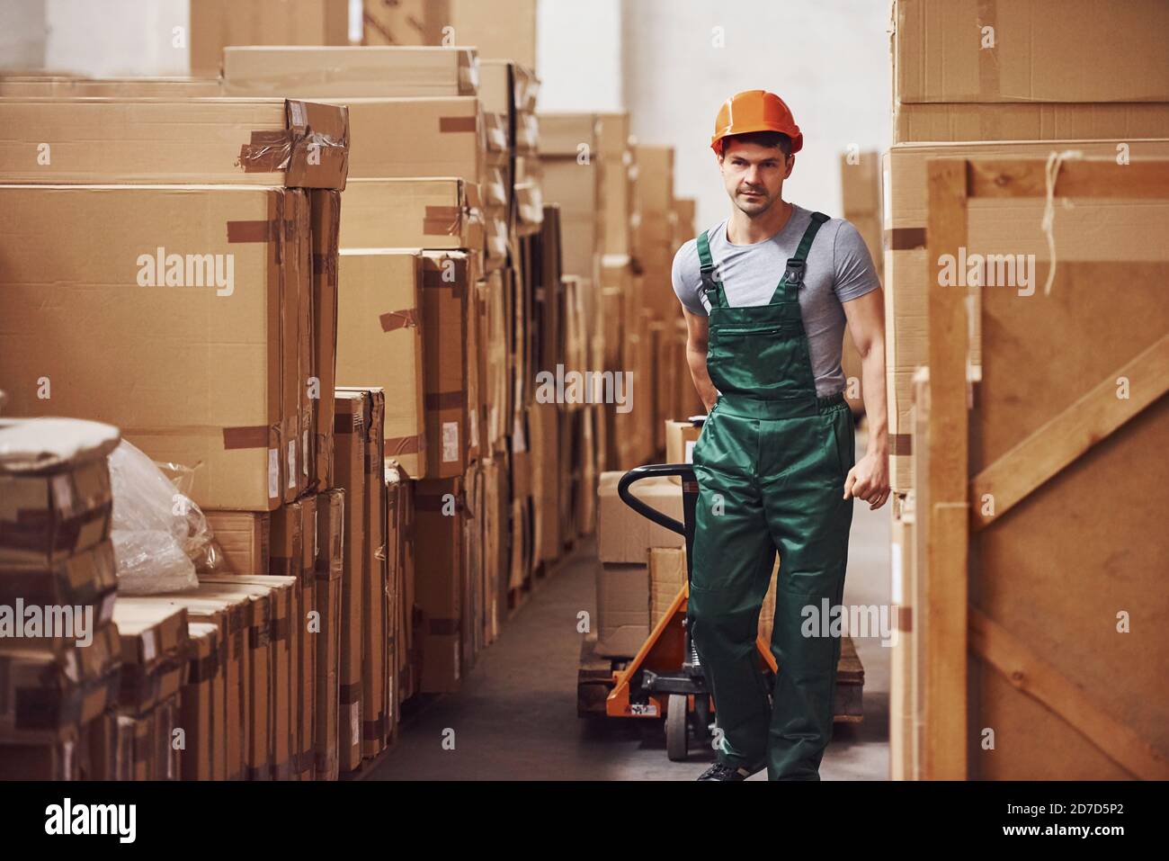 Young male worker in uniform is in the warehouse with pallet truck ...