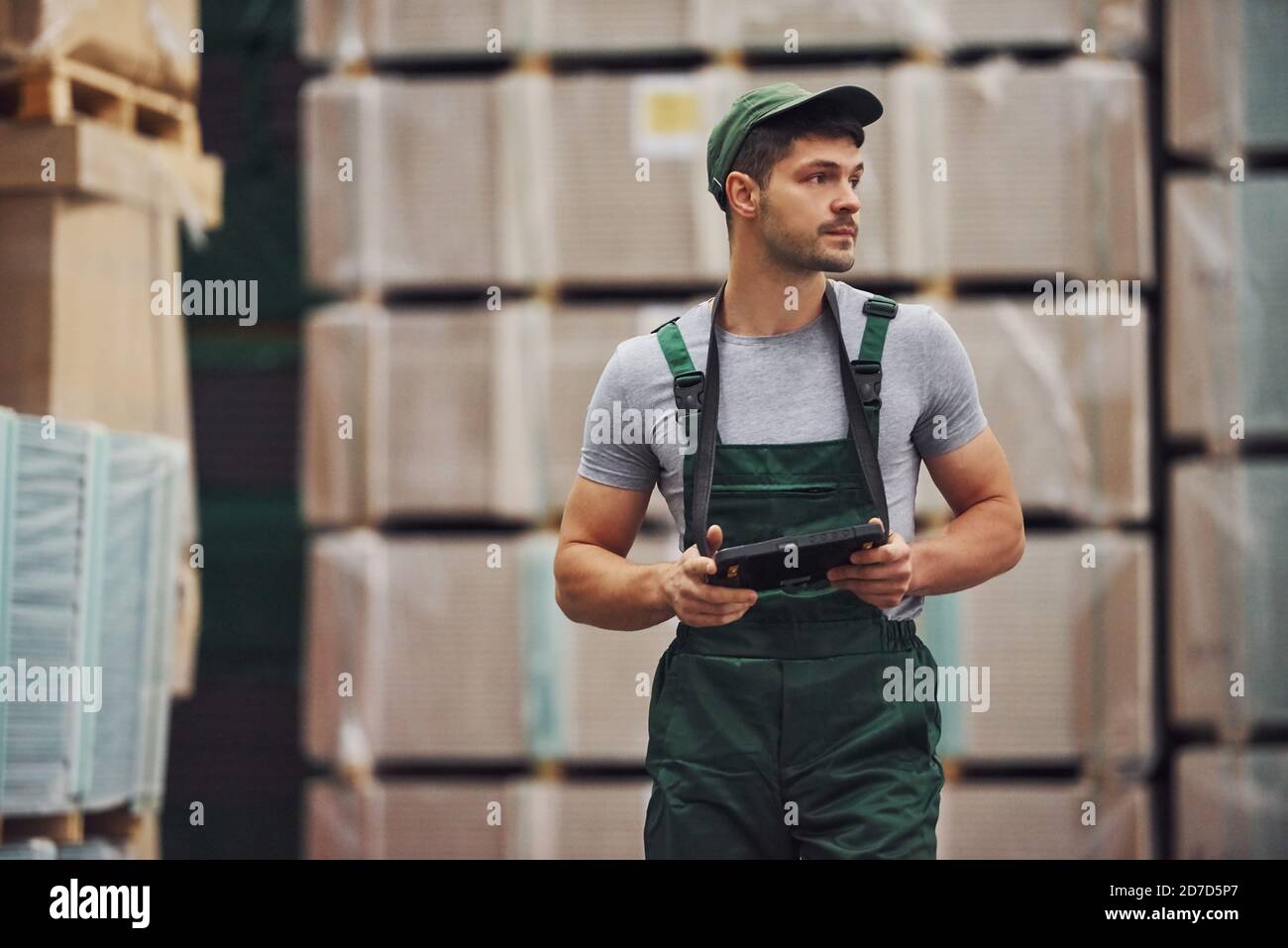 Storage worker in green colored uniform and notepad in hands checks ...
