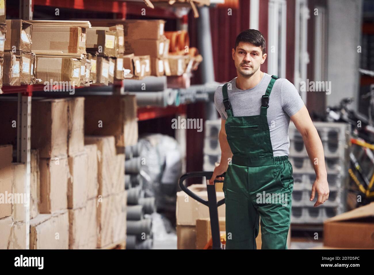 Young male worker in uniform is in the warehouse with pallet truck ...