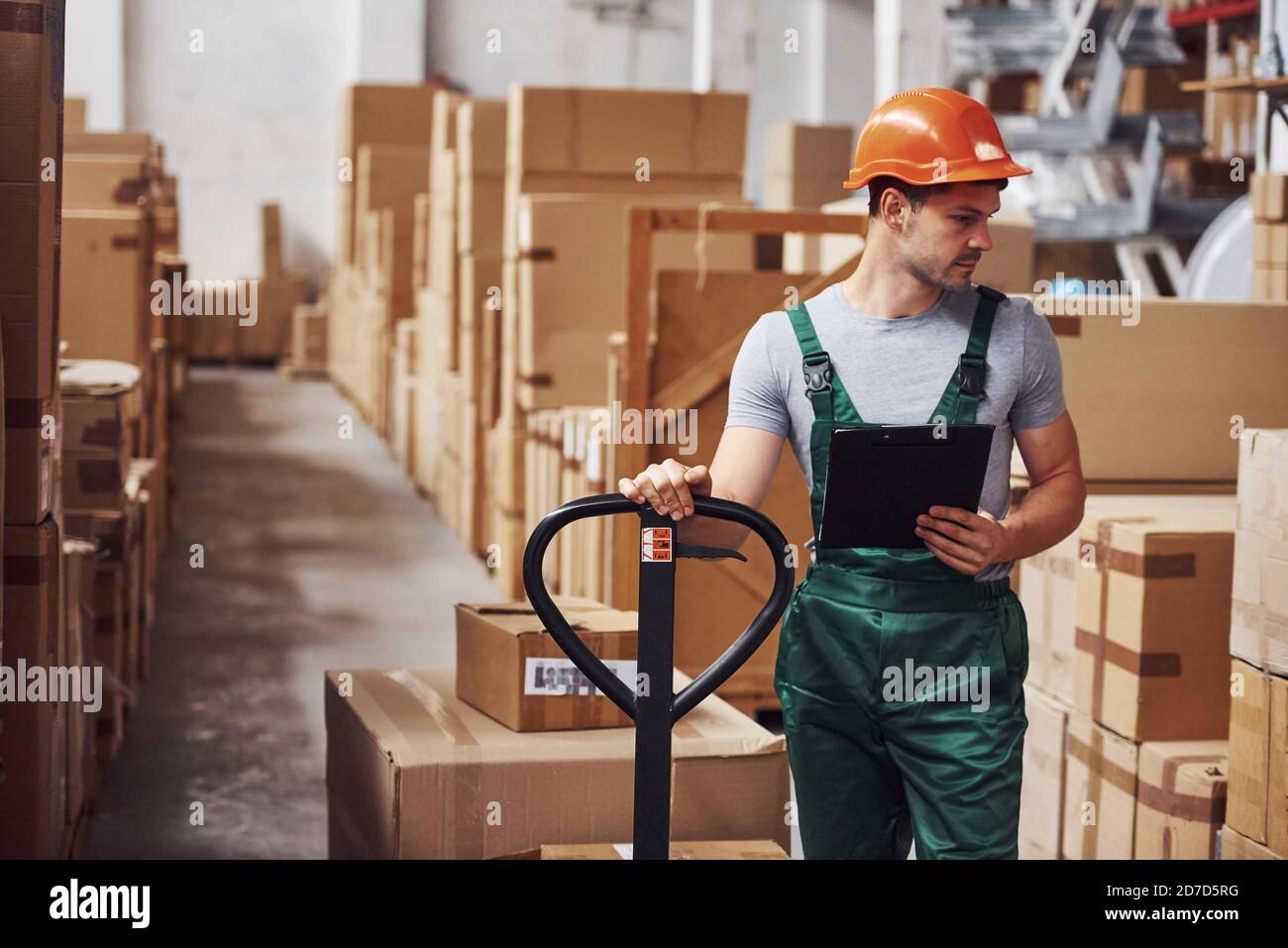 Young male worker in uniform is in the warehouse with notepad and ...