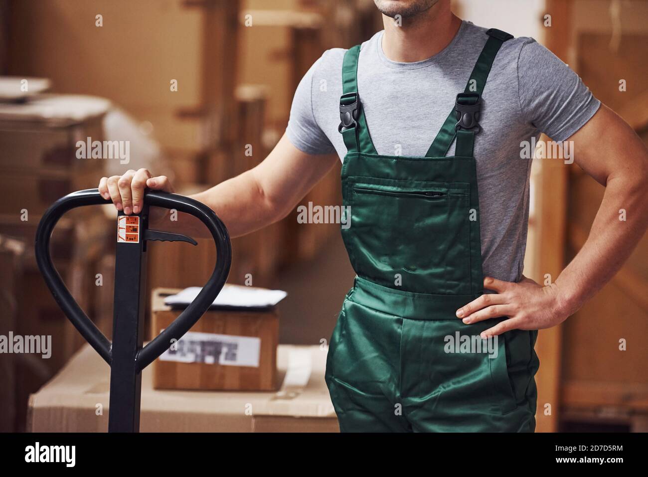 Young male worker in uniform is in the warehouse with pallet truck ...