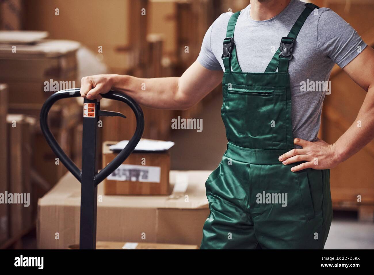 Young male worker in uniform is in the warehouse with pallet truck ...