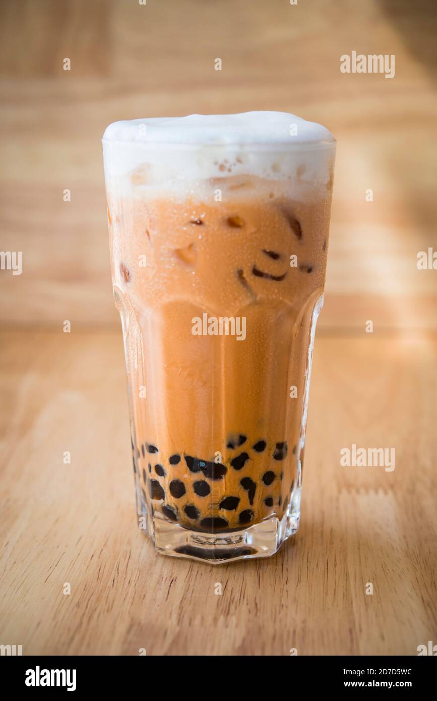 Aisian style orange bubble tea with milk froth on top on a wood ...