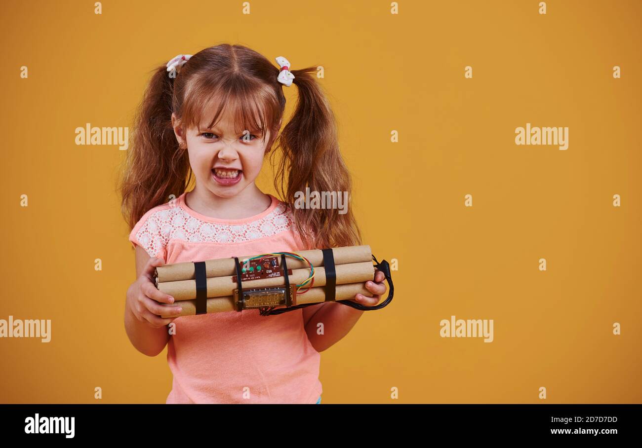 Little girl with explosive in the studio against yellow background ...