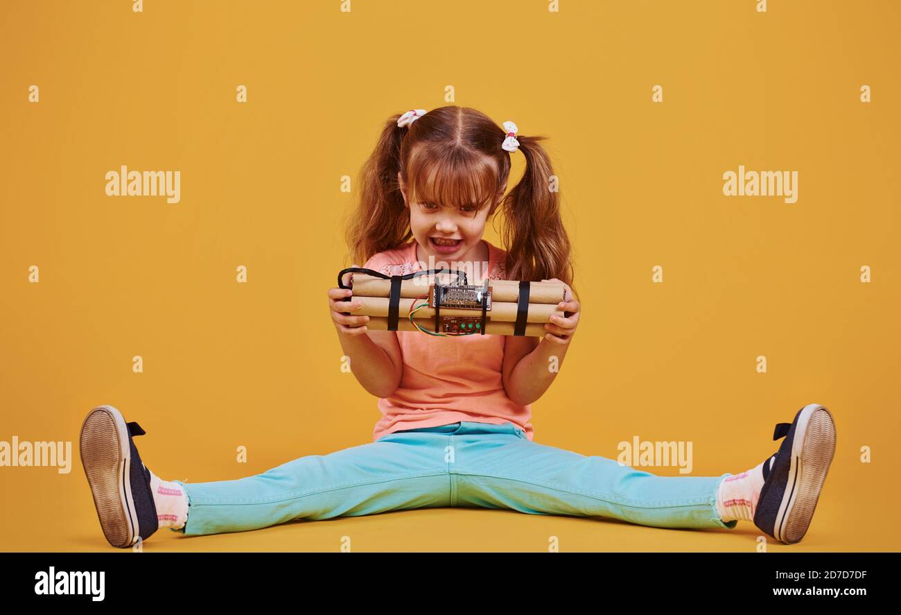 Little girl with explosive in the studio against yellow background ...