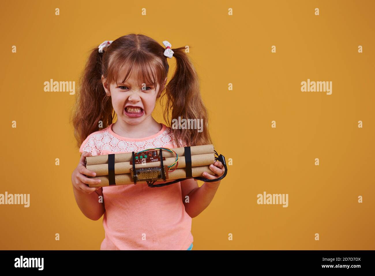 Little girl with explosive in the studio against yellow background ...