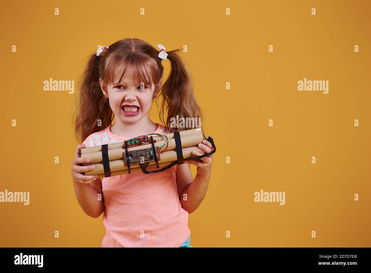 Little girl with explosive in the studio against yellow background ...