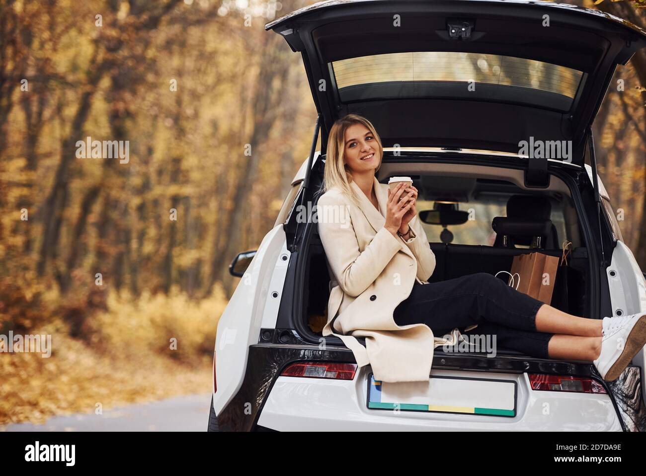 Girl sits on the back of car. Modern brand new automobile in the forest ...